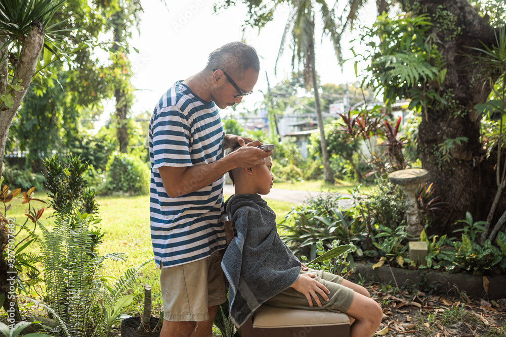 A man giving a boy a mohawk haircut in the garden during the community ...
