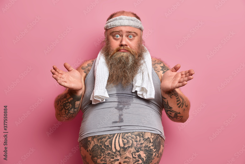 Puzzled bearded man with excess weight, spreads palms and looks ...