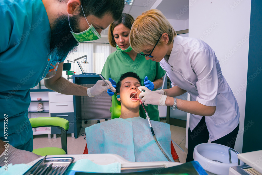 Team of dentists treating the teeth of their young boy patient using ...
