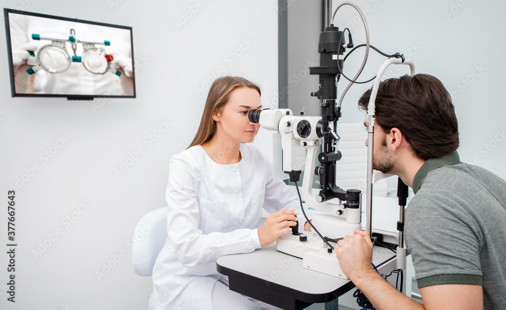 Eye doctor woman is doing a diagnostic vision exam adult man. Eye exam ...