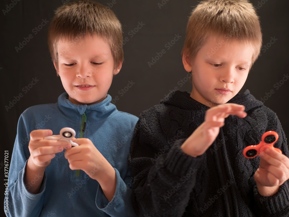 Two funny blond children in dark shirts twists spinner on his nose ...