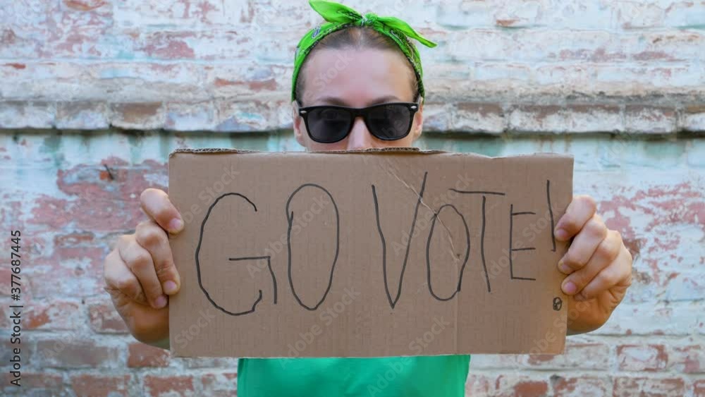 Girl shows cardboard with Go Vote! sign on brick wall urban background ...