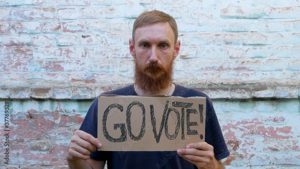 Man shows cardboard with Go Vote sign on brick wall urban background ...