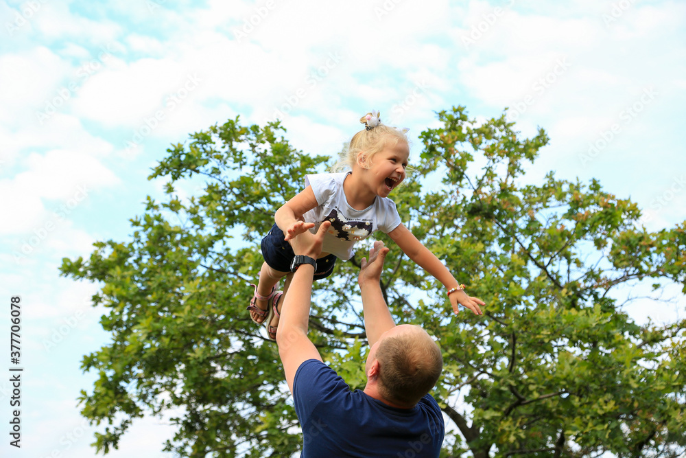 A father tosses his three-year-old daughter over his head. The daughter ...