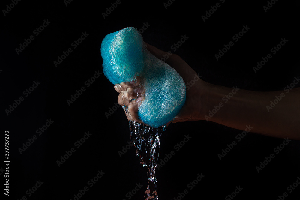 Water on a black background. Water is squeezed out of the bath sponge ...