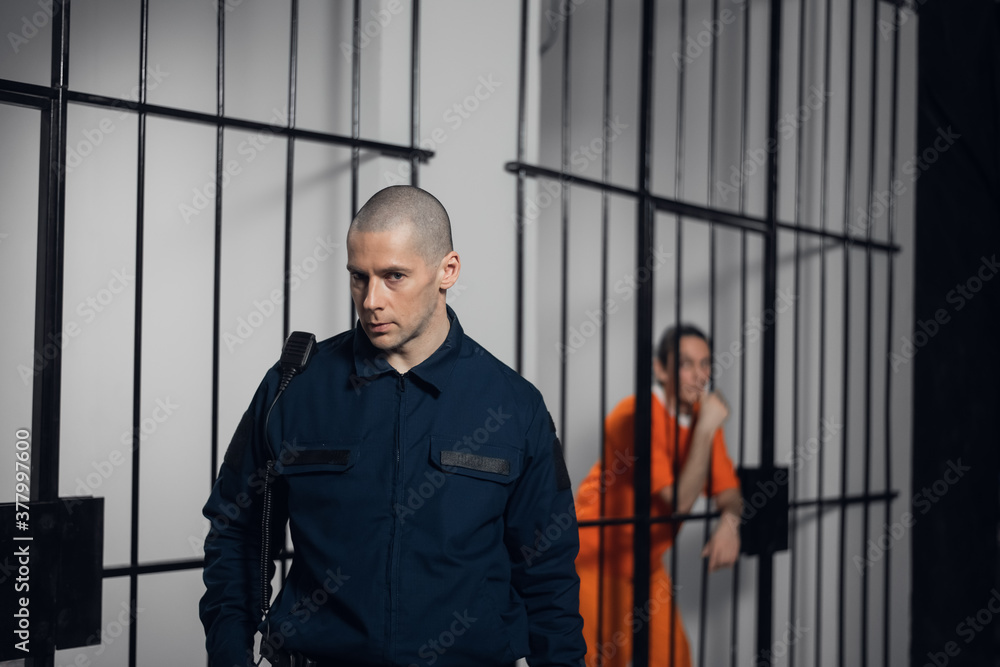 A strict prison guard in uniform guards cells with prisoners in a ...