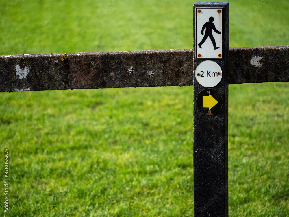 Sign on a fence walking man and direction arrow to the right. and 2 km ...