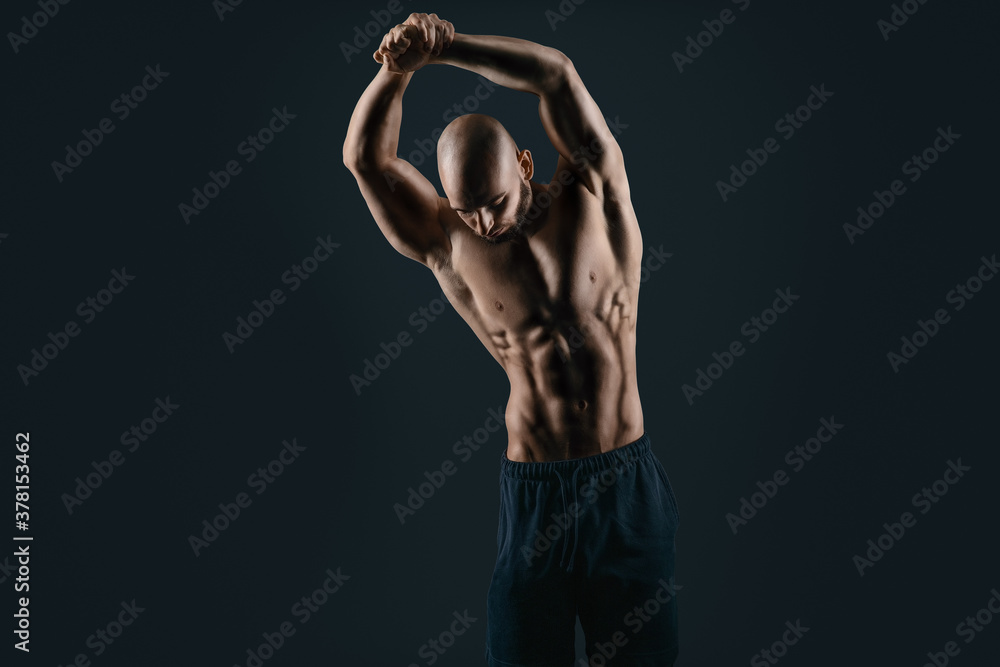 young bodybuilder look down isolated on black stretch his arms above ...