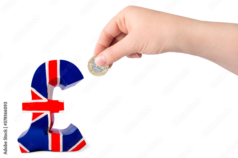 A female hand putting a one pound British coin into a piggy bank shaped ...
