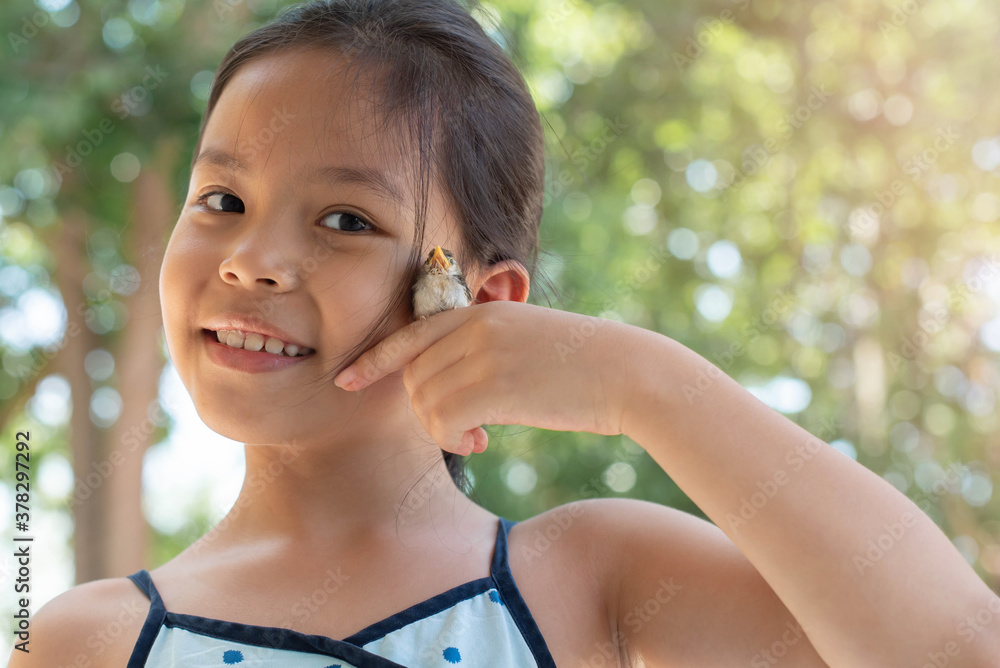 adorable little girl and bird sitting on her finger..portrait Asian cute child girl is feeding ...