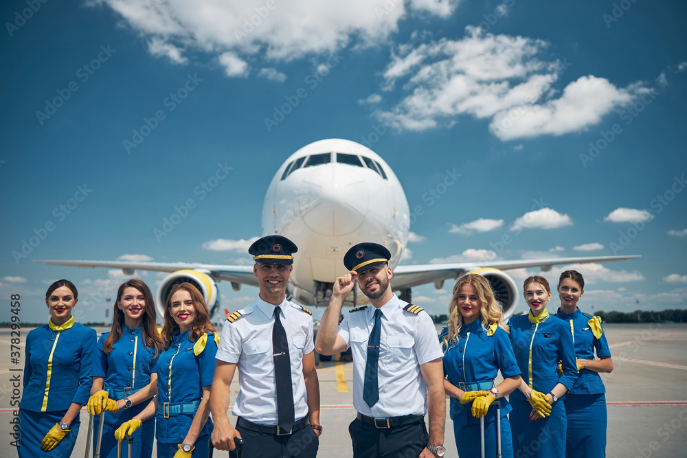 Cheerful airline workers standing in airfield under blue sky Stock ...