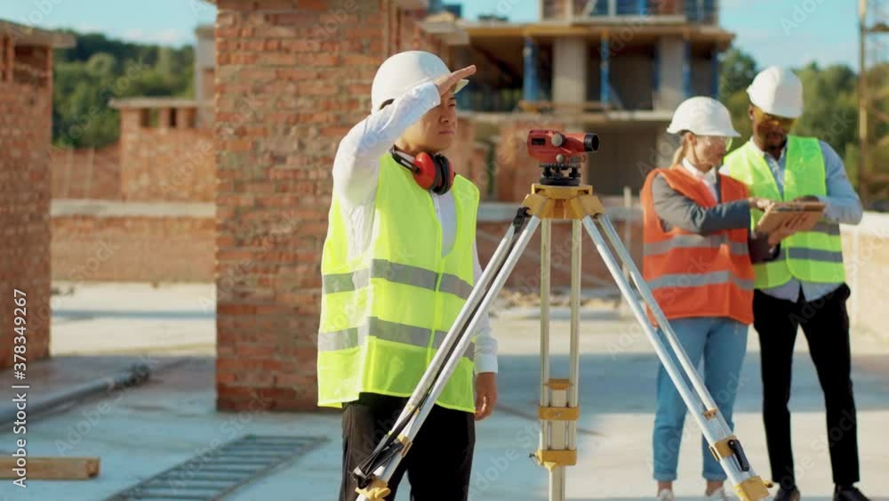 Young asian man engineer surveyor takes measures with theodolite stand helmet hardhat geodesy ...
