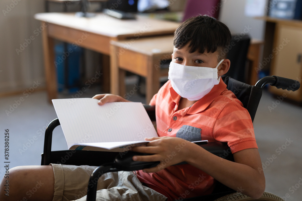 Portrait of disable boy wearing a face mask sitting in his wheelchair ...