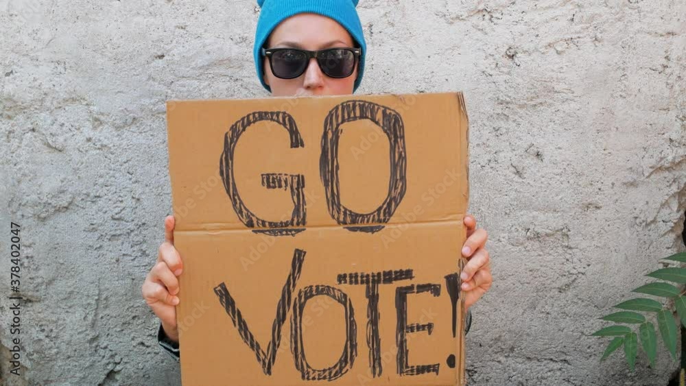 Stockvideon Woman shows cardboard with Go Vote sign on brick wall urban ...