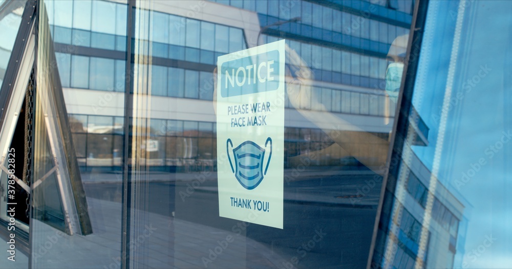 Female wearing face mask placing COVID-19 face mask poster on a window ...