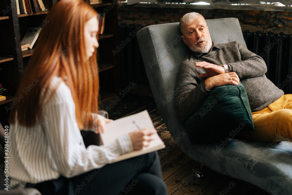 Serious red-haired young woman psychologist taking notes in notebook ...