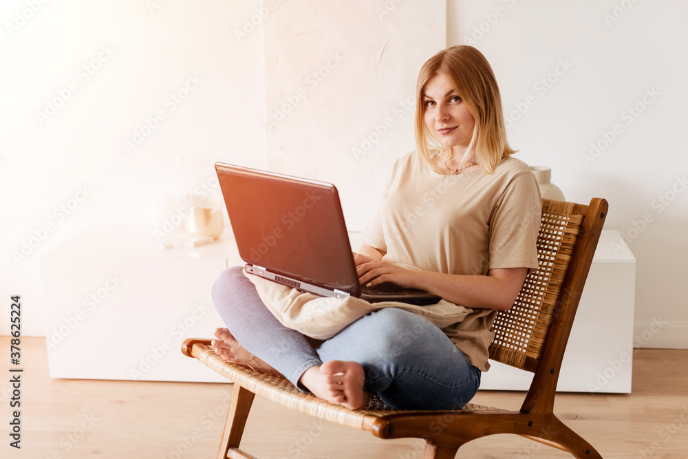 Blondie girl works at the laptop computer, sitting on the armchair in ...