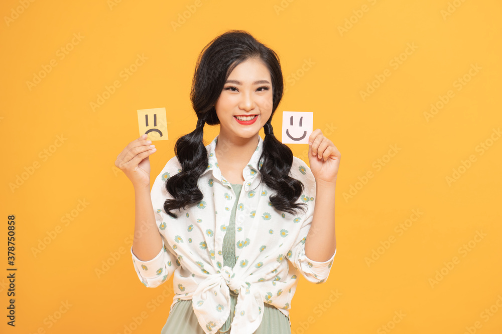 Young woman holding sticky paper note with sad, smiley face emoticon ...