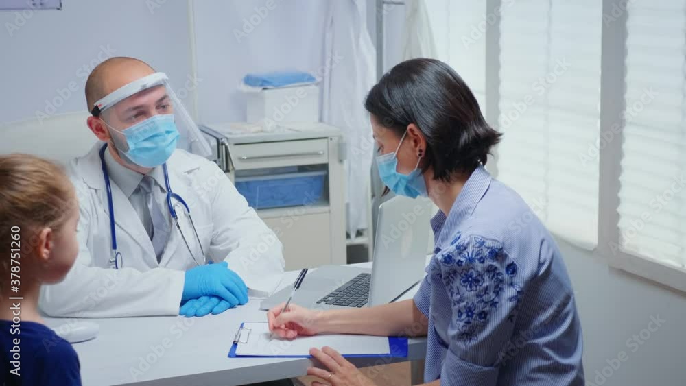 Mother writing on clipboard doctor instructions wearing protection mask ...