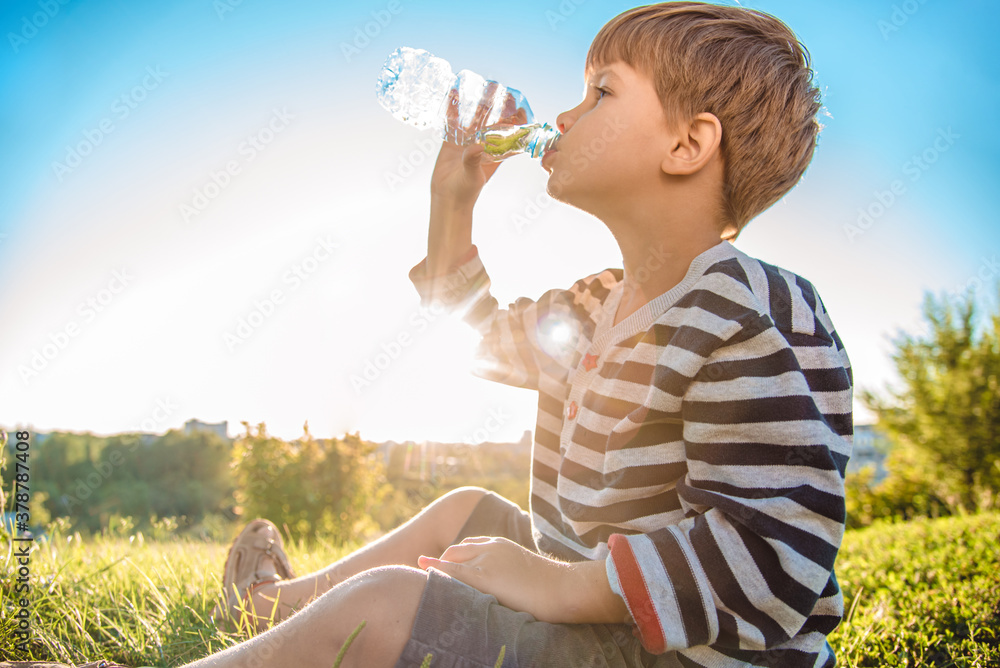 Foto de Cute boy sitting on the grass drinks water from a bottle in the ...