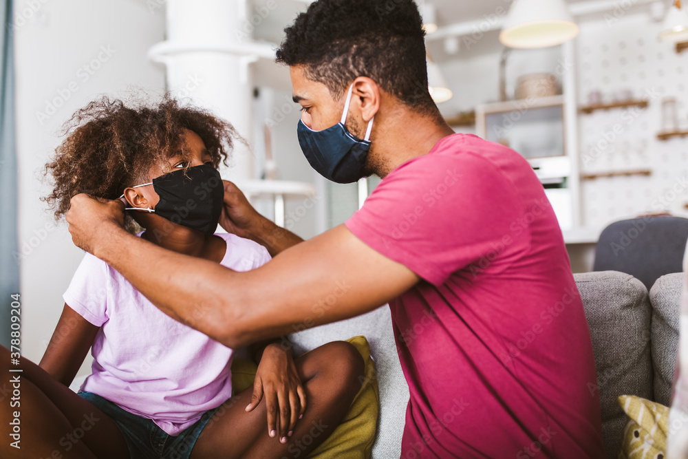 Father in a medical mask puts a protective mask on his daughter at home ...