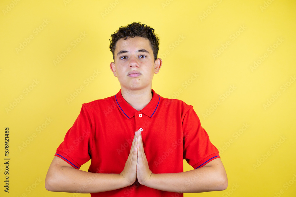 Beautiful teenager boy over isolated yellow background begging and ...