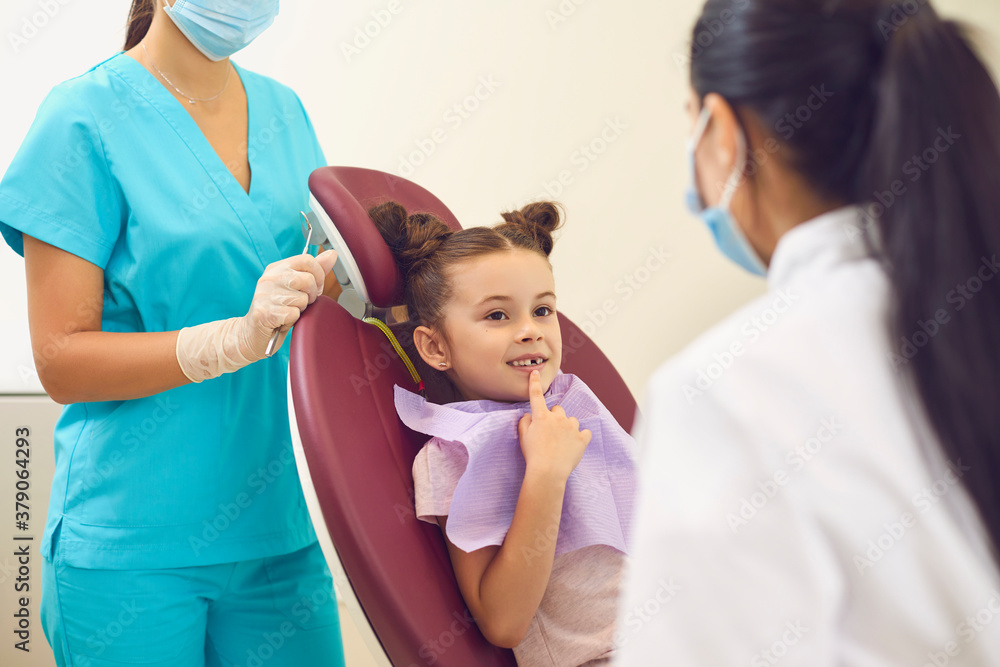 Smiling girl sitting in dental chair and showing front teeth to dentist ...