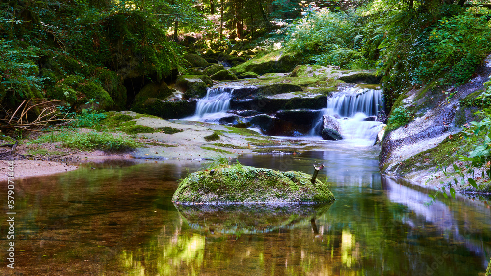 Green stone with rusty clamp in shallow water, cascades of a waterfall ...