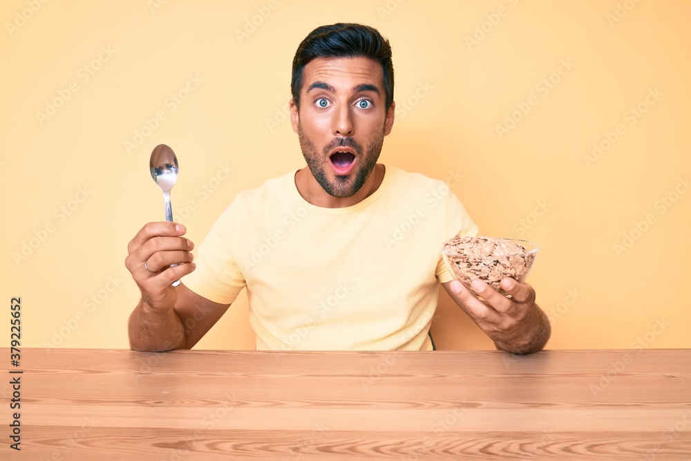 Young handsome hispanic man eating healthy whole grain celears sitting ...