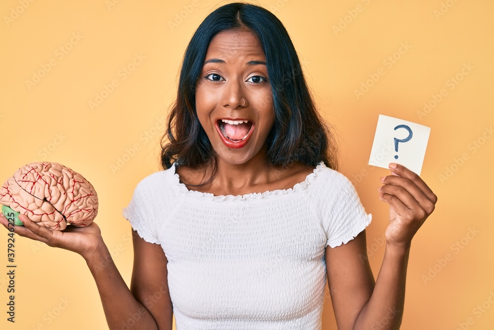 Young indian girl holding brain and question mark reminder smiling and ...