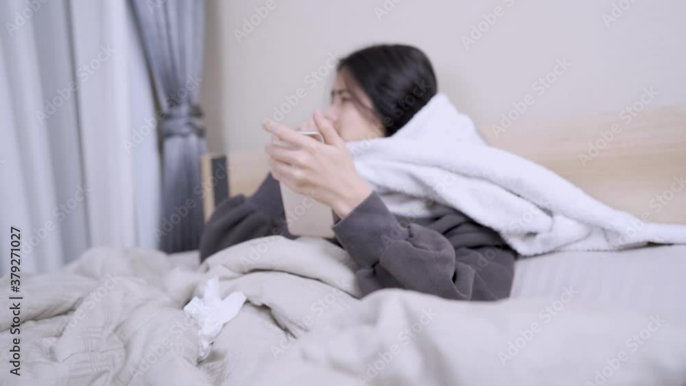 Young asian woman lying down inside blankets using smartphone, cold ...