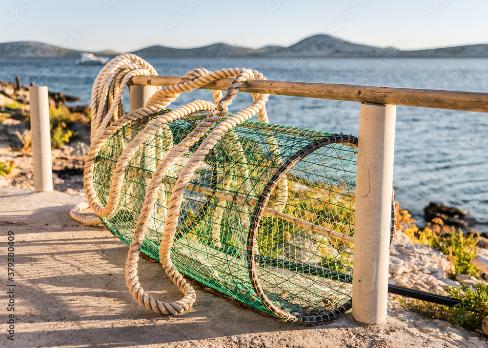 Cylindrical fish trap with ropes drying on the shore near the village ...