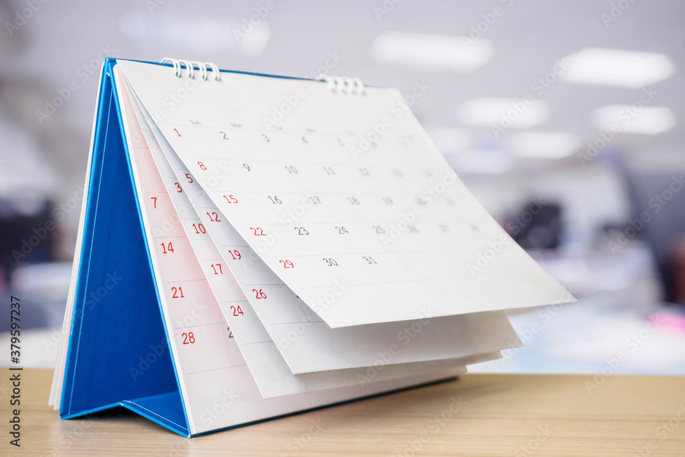 Calendar page flipping sheet on table with blurred office interior ...