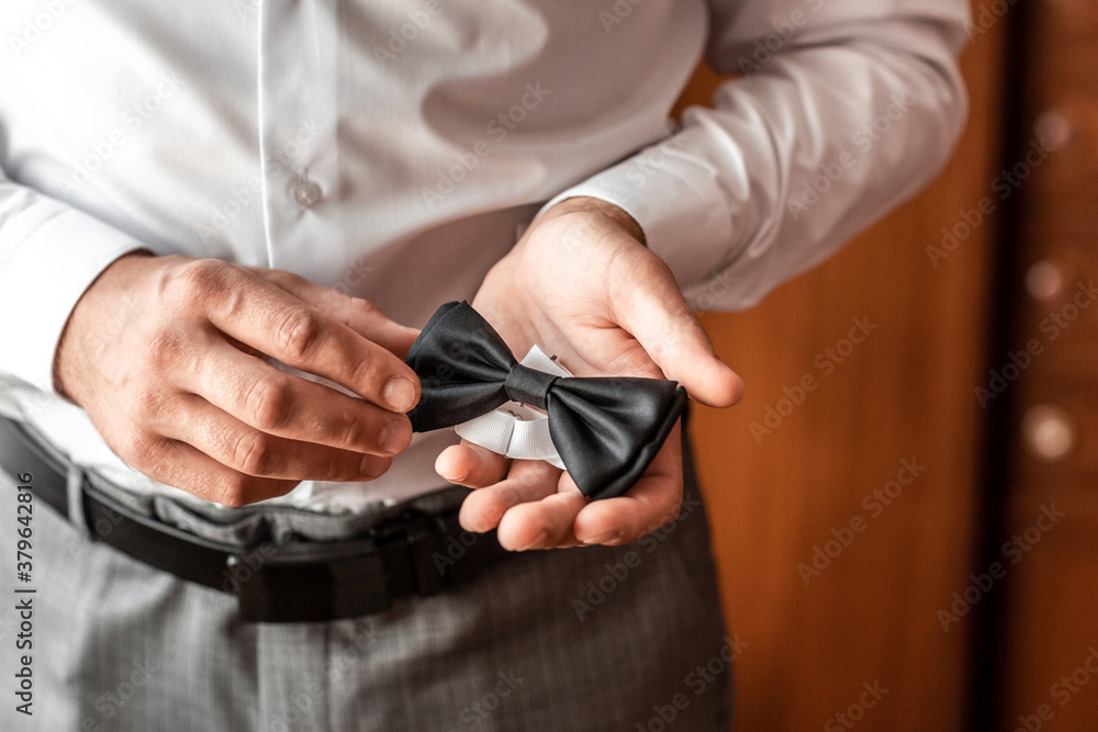 The handsome groom tying his bow-tie in the morning of the wedding day ...
