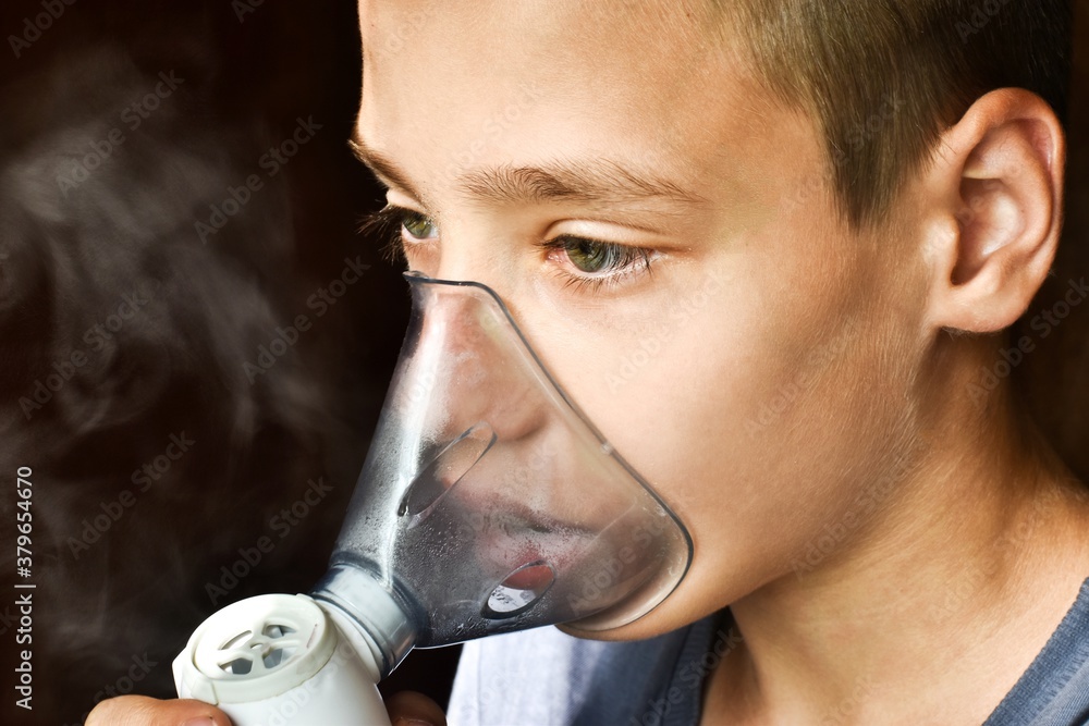 The boy is breathing into the nebulizer.The boy is doing inhalation at ...