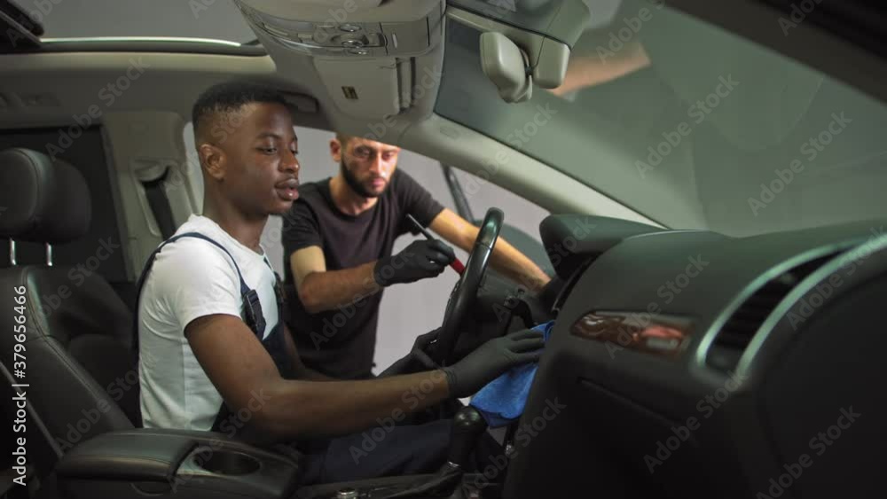 african american at work in the car wash cleans the car, a cheerful guy ...