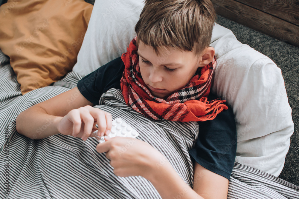 Sick teenage boy with flu is sneezing and coughing on the bed ...