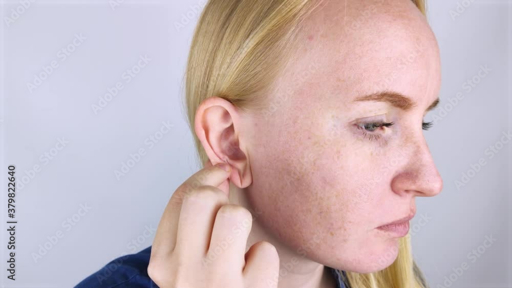 A woman on a white background shows her ear. The macro video shows the ...