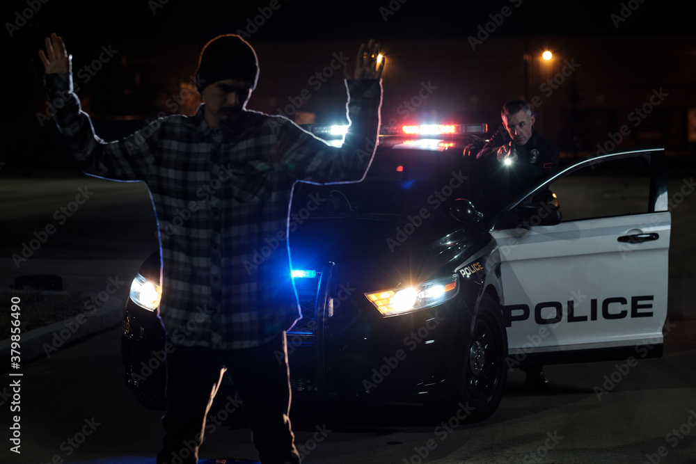 A suspect stands with raised hands as a Police Officer has his gun ...