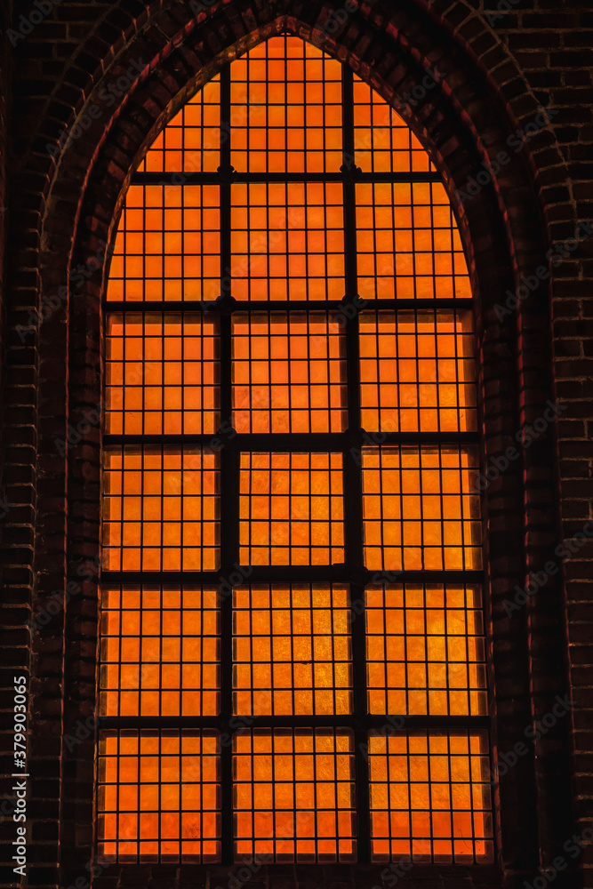 Deep orange light coming from a church 's Gothic window conveys a ...