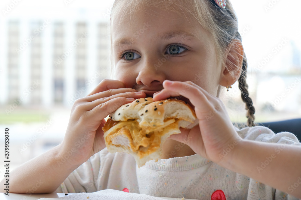 Foto de Little girl eating hamburger in a fast food restaurant. Child ...