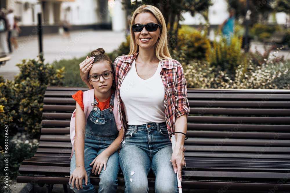 Young blind mother sitting in schoolyard with her little daughter. They ...