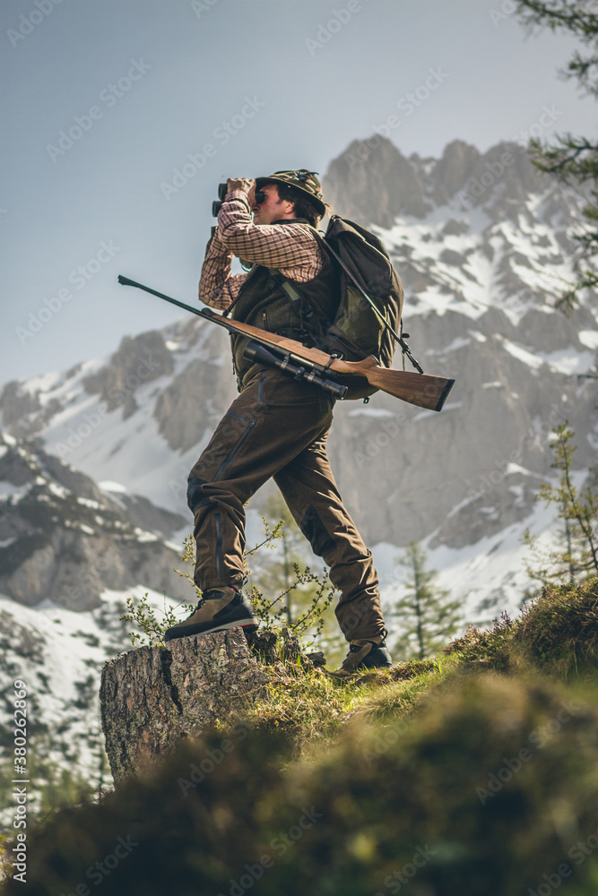 hunter standing on a trunk with his shotgun looking through binocular ...