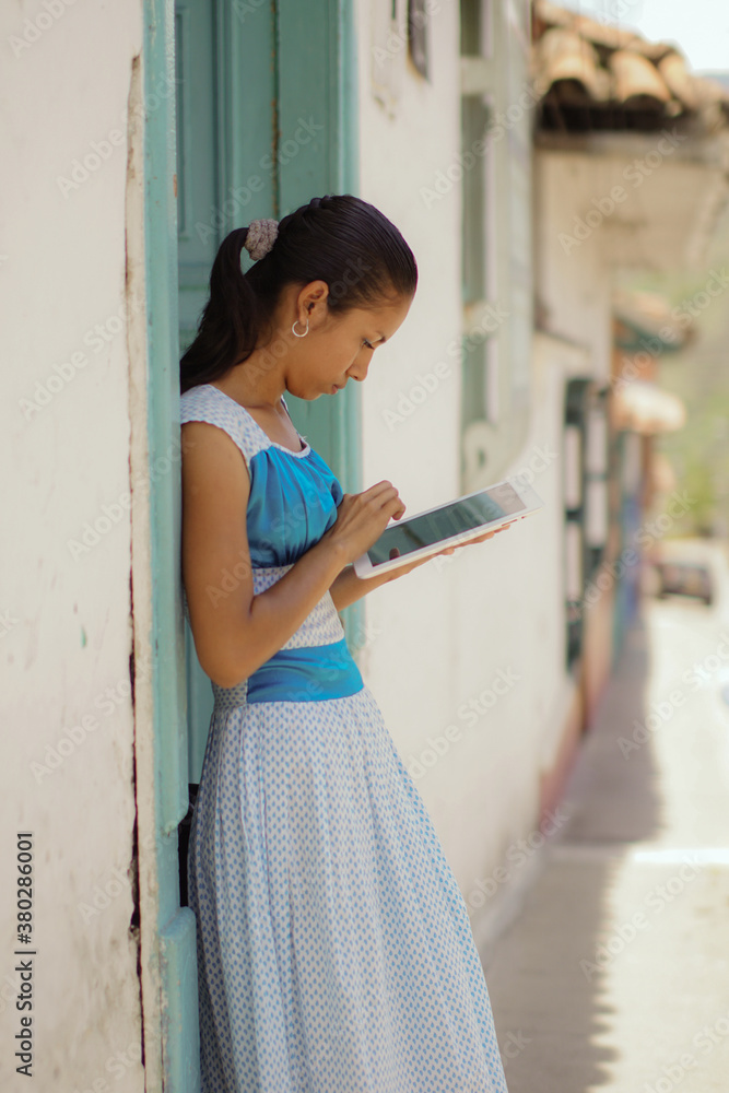 Foto de Young attractive latin woman in dress using tablet outdoors do ...