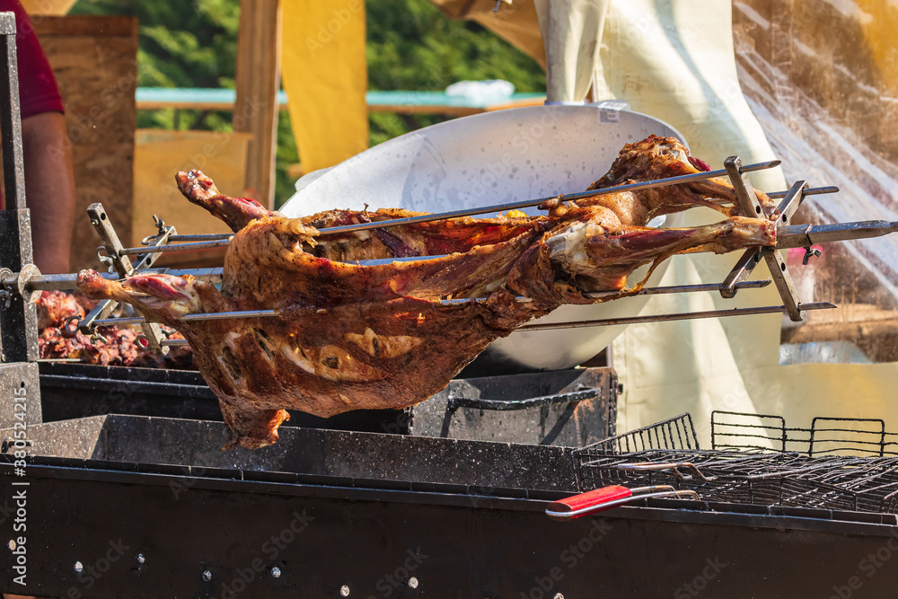 The carcass of a young sheep roasting on a spit over a low fire of ...