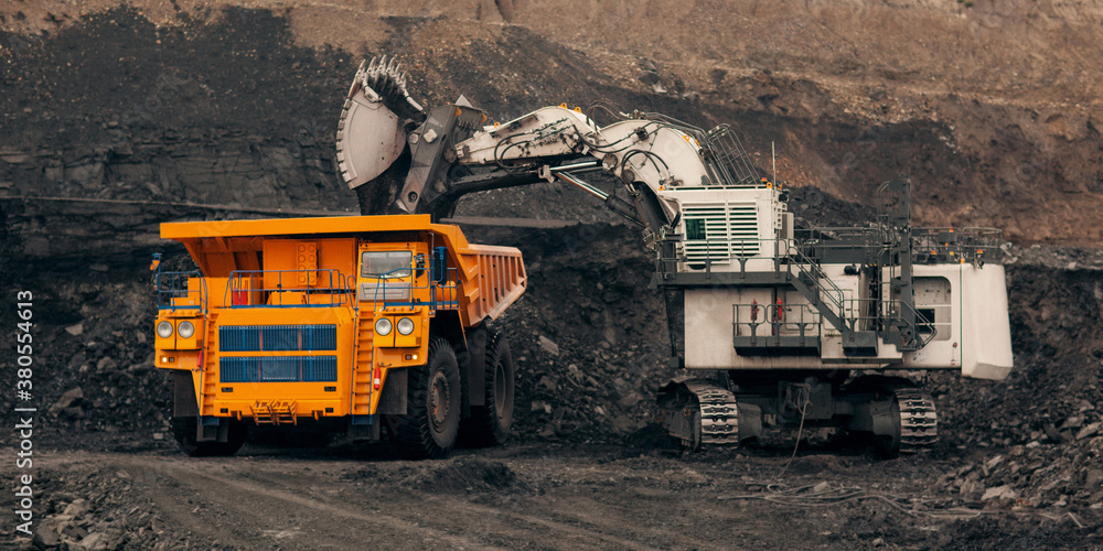 A huge excavator loads rock formation into the back of a heavy mining ...