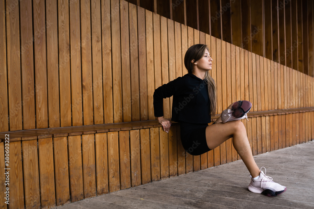 A girl in a black sports uniform does reverse push-ups with support on ...