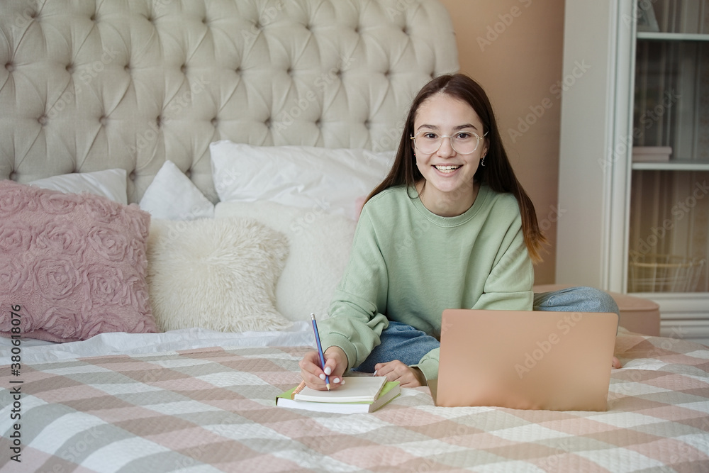 Cute teenager girl doing homework sitting on bed at home. Young pretty ...