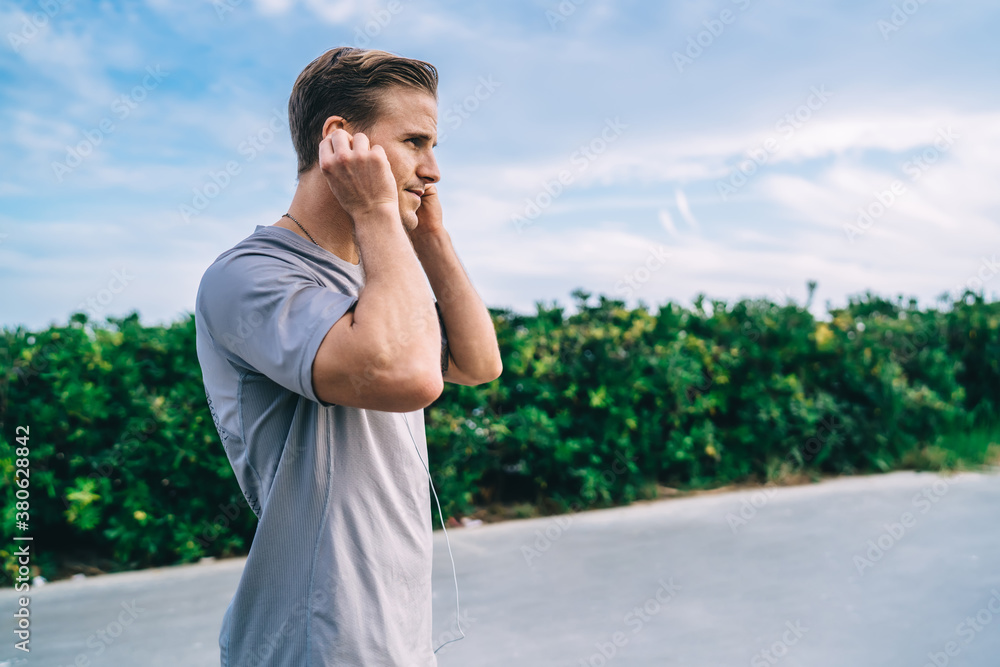 Caucasian muscular sportsman wearing electronic earphones getting ready ...
