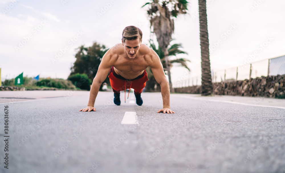 Strong Caucasian sportsman with muscular body shape doing push ups on ...
